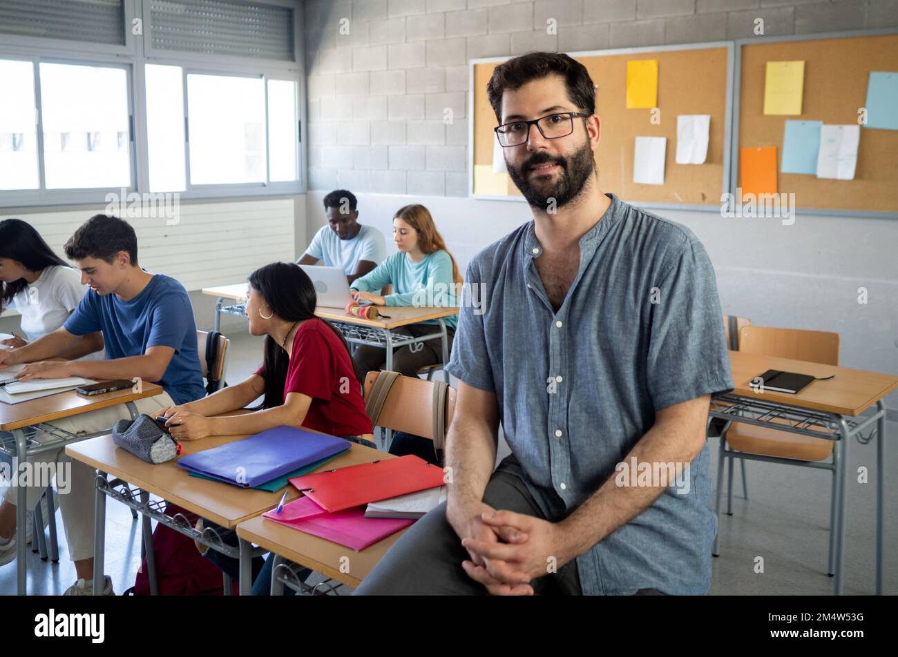Portrait of a male teacher looking at camera in a class with students ...