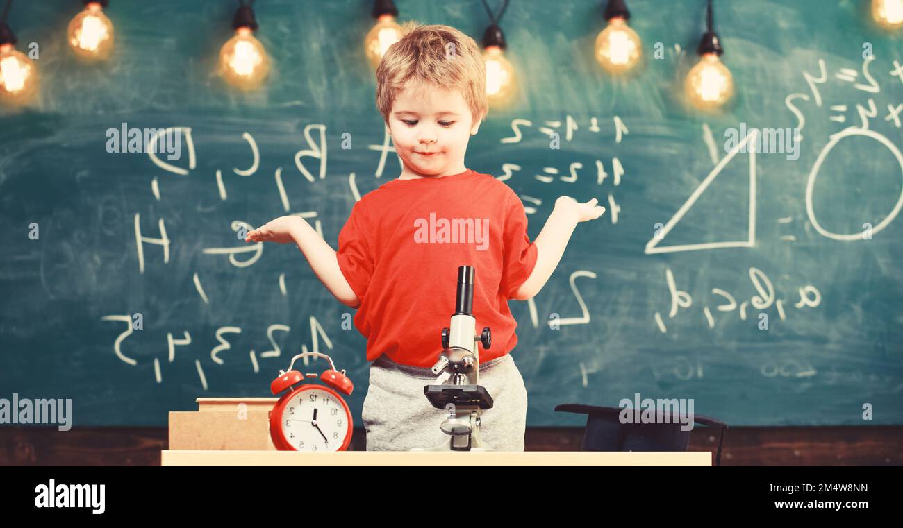 Kid boy near microscope, clock in classroom, chalkboard on background ...