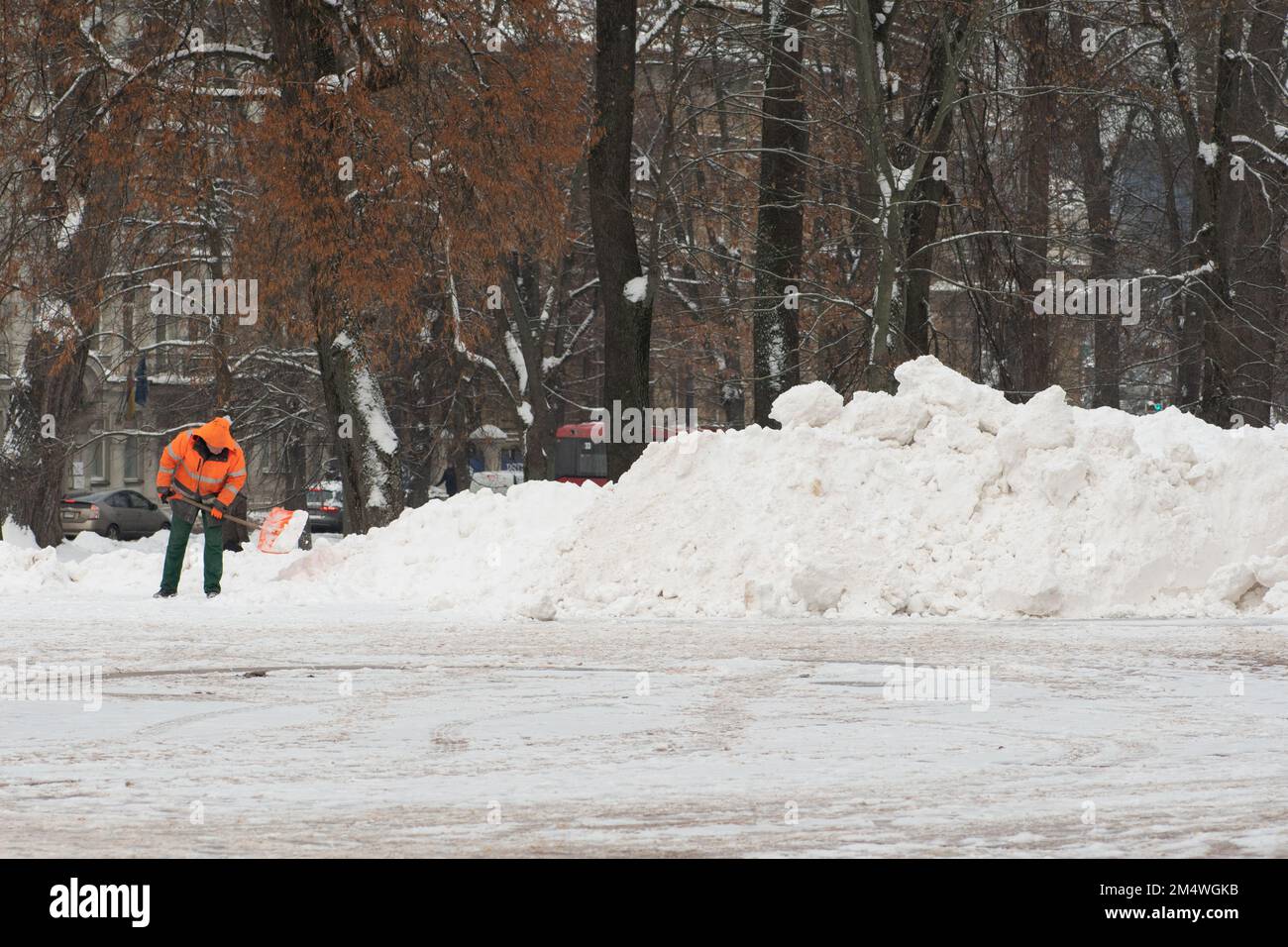 Workman with shovel at work in winter clearing snow in the square after ...