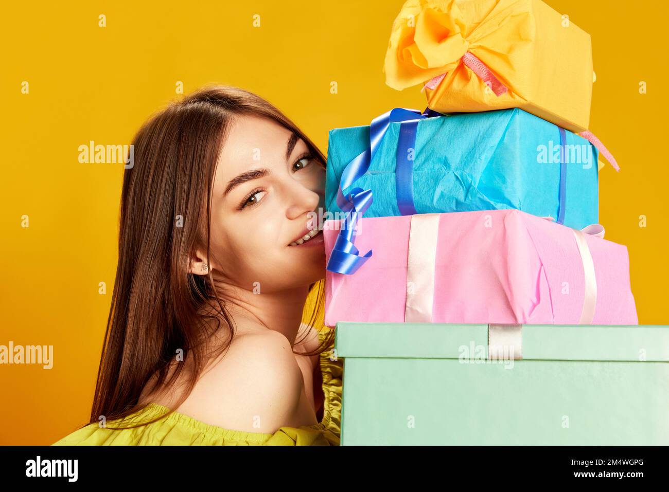 Portrait of young beautiful girl in cute dress posing with many present ...