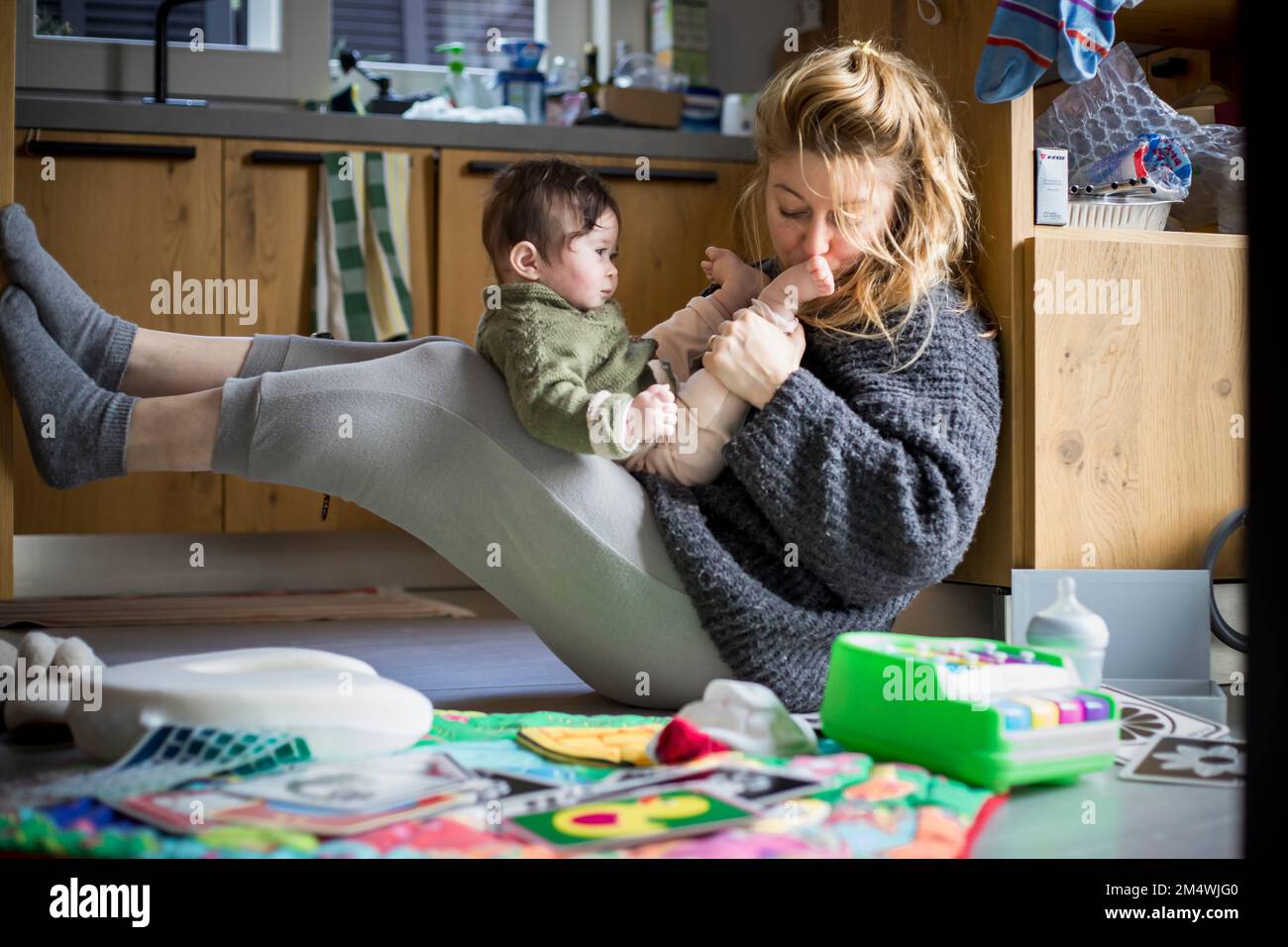 The young mother, kissing the feet of her baby on her knees, spends ...