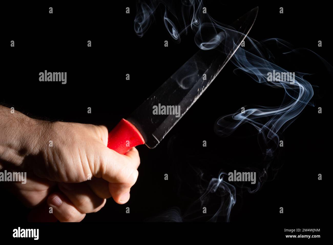 A male hand holding a sharp silver knife with smoke on black background ...