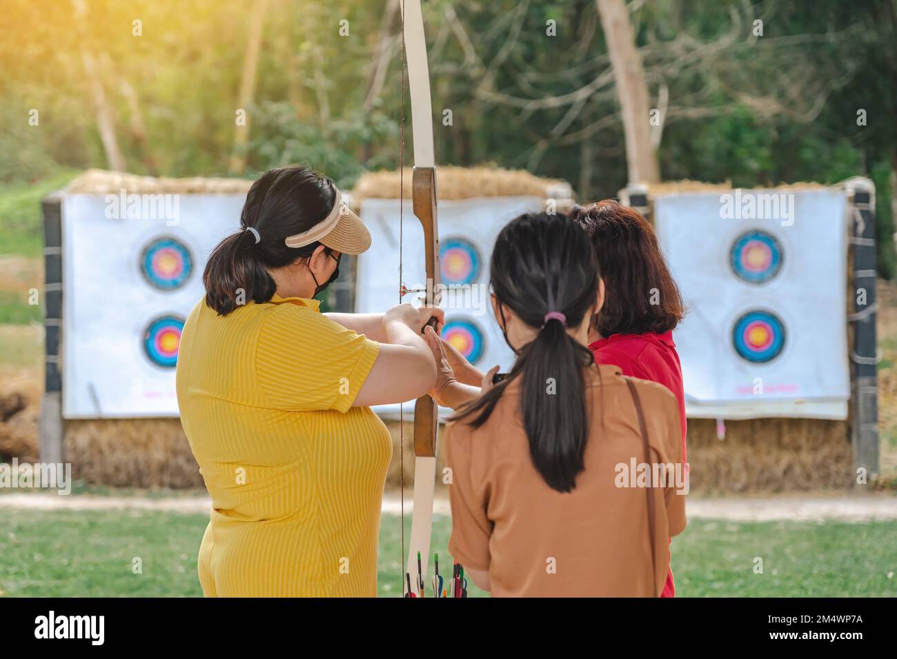 Back view of Asian woman wear visor with face mask aims archery bow and ...