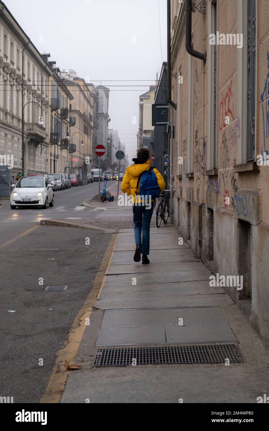 A vertical of a man with a blue backpack walking in the narrow streets ...