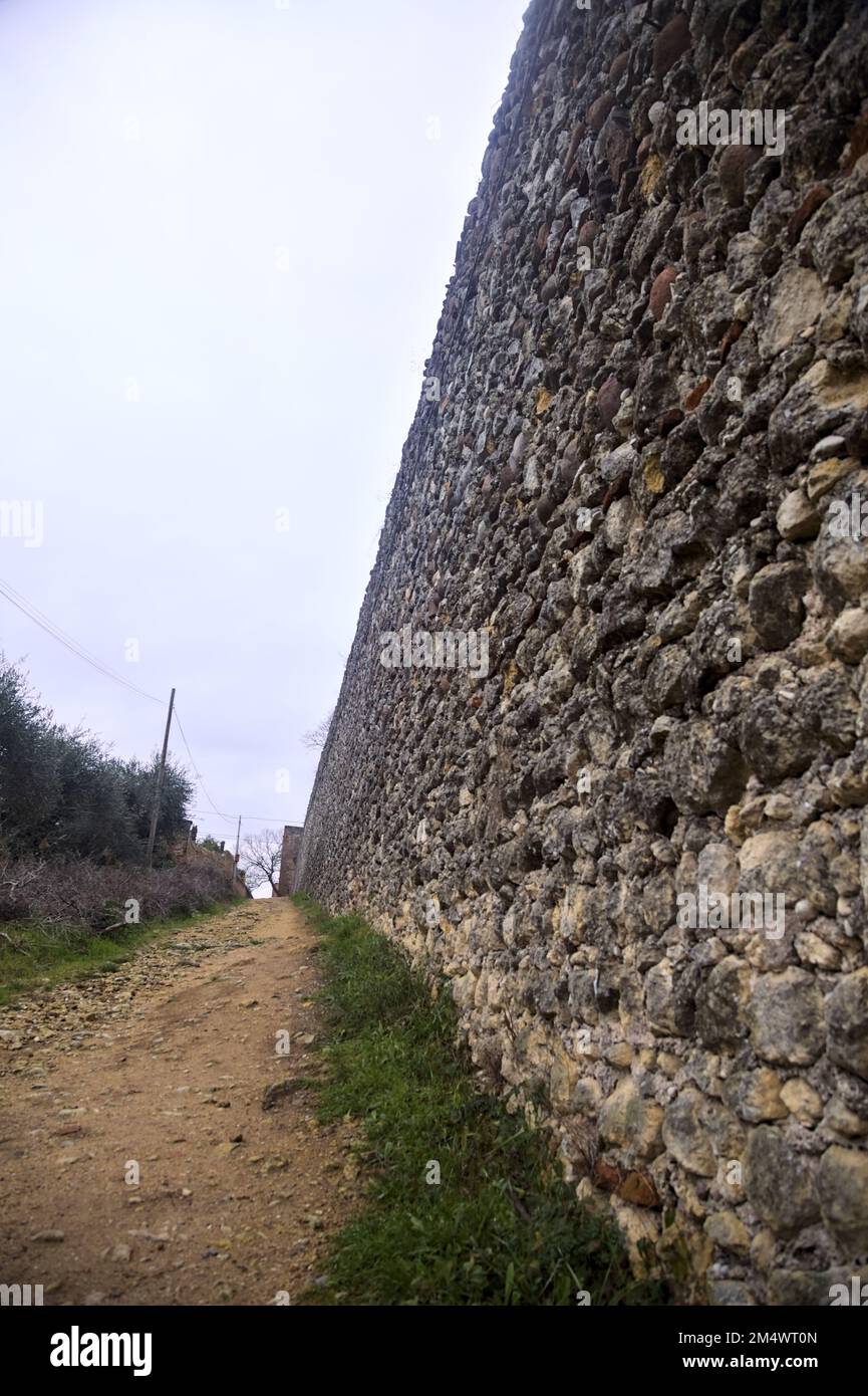Dirt path next to a stone fortification and olive trees with ...