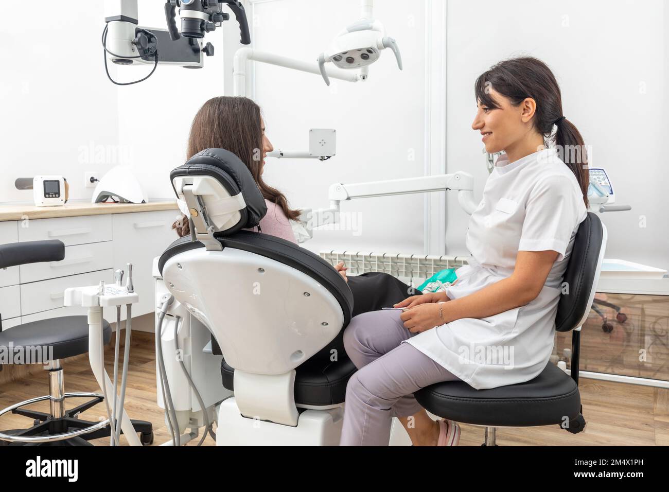 Female dentist talking to a young patient during appointment in modern ...