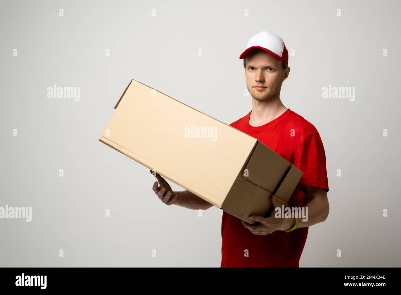 Image of bearded curly delivery man in red uniform with a blank cardboard, percel on white ...