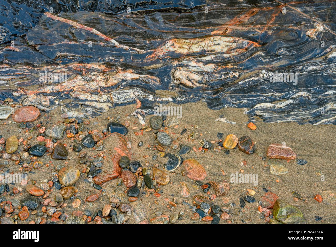 Incoming waves, wet sand and a rock outcrop with igneous intrusions ...