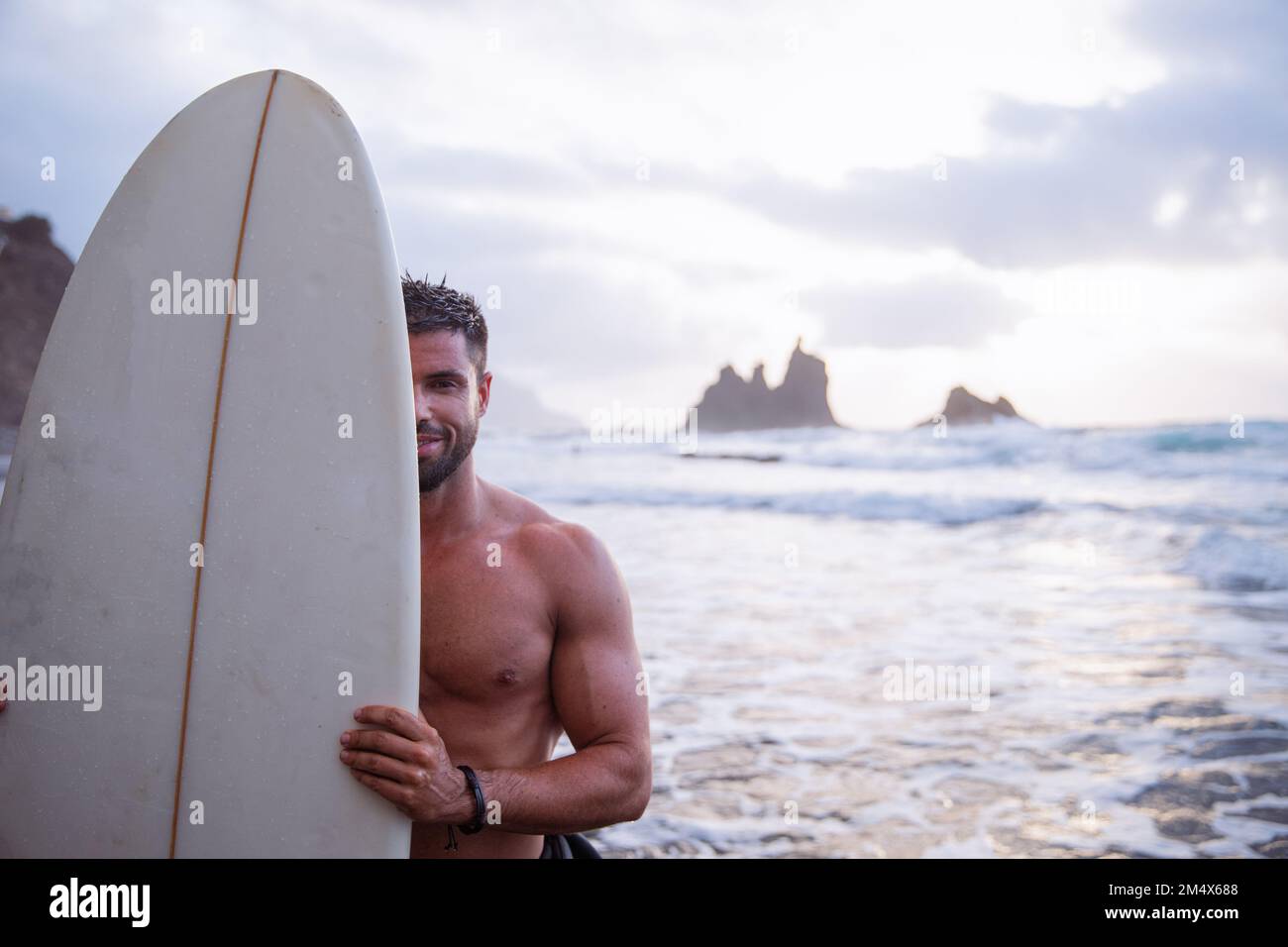 Smiling surfer covers half of his face with surfboard, extreme sports ...