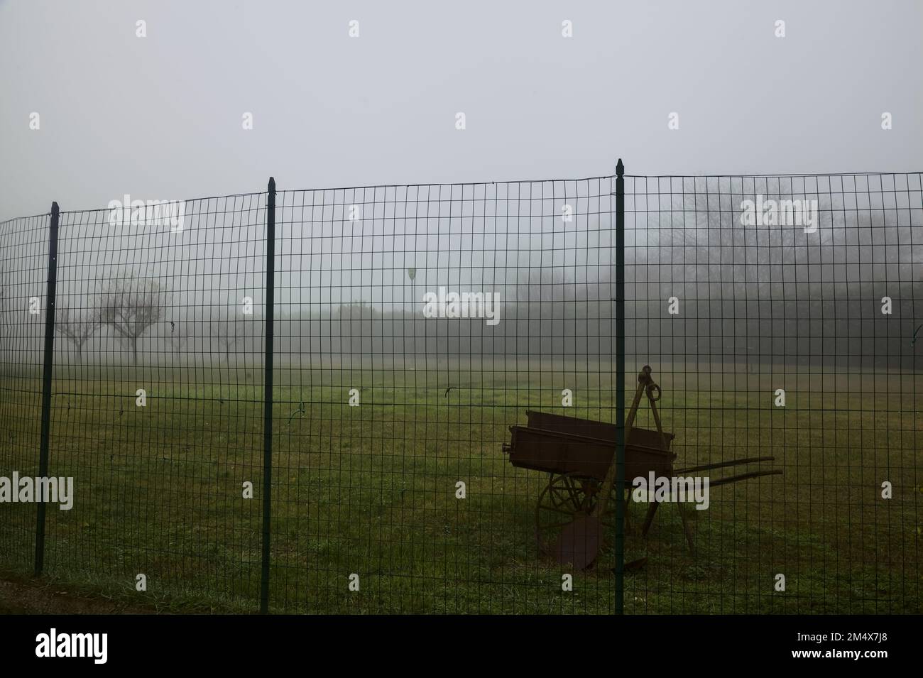 Wheelbarrow and plow on a lawn behind a fence on a foggy day Stock ...