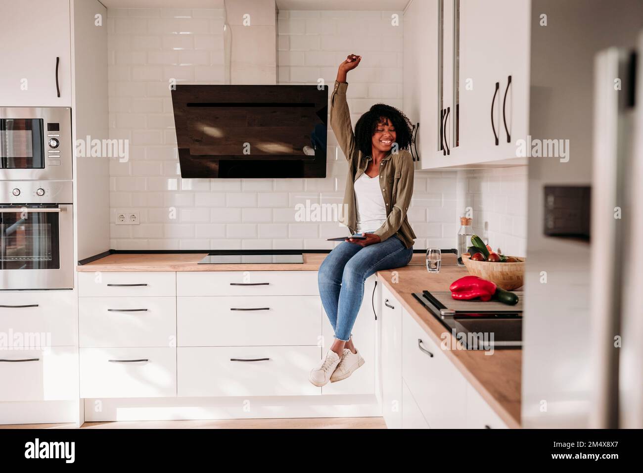 Woman with hand raised sitting on kitchen counter at home Stock Photo ...