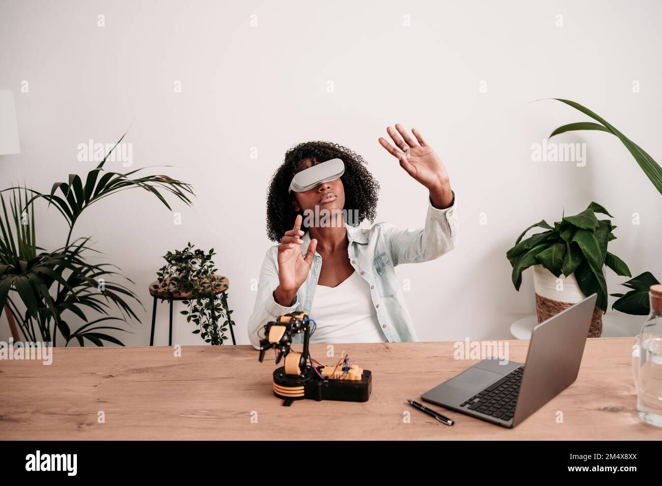 Businesswoman wearing virtual reality headset with robotic arm on desk ...