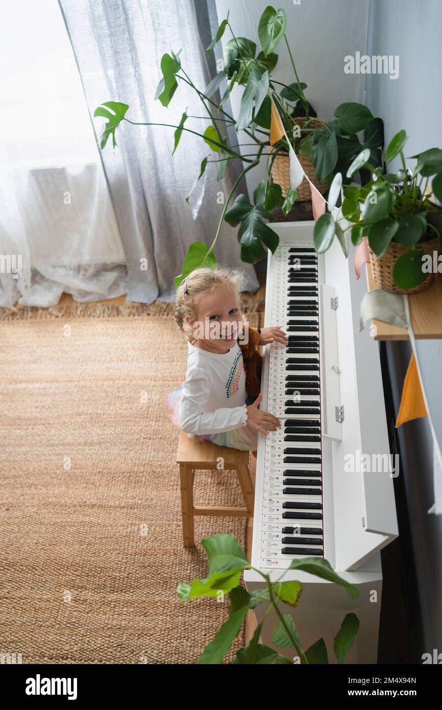 Happy girl playing piano amidst plants at home Stock Photo - Alamy