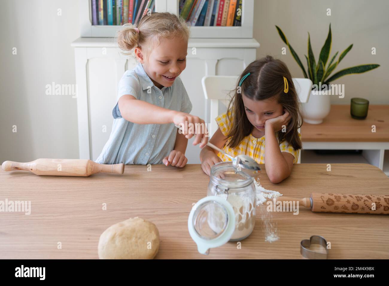 Happy girl pouring flour on table with friend at home Stock Photo - Alamy