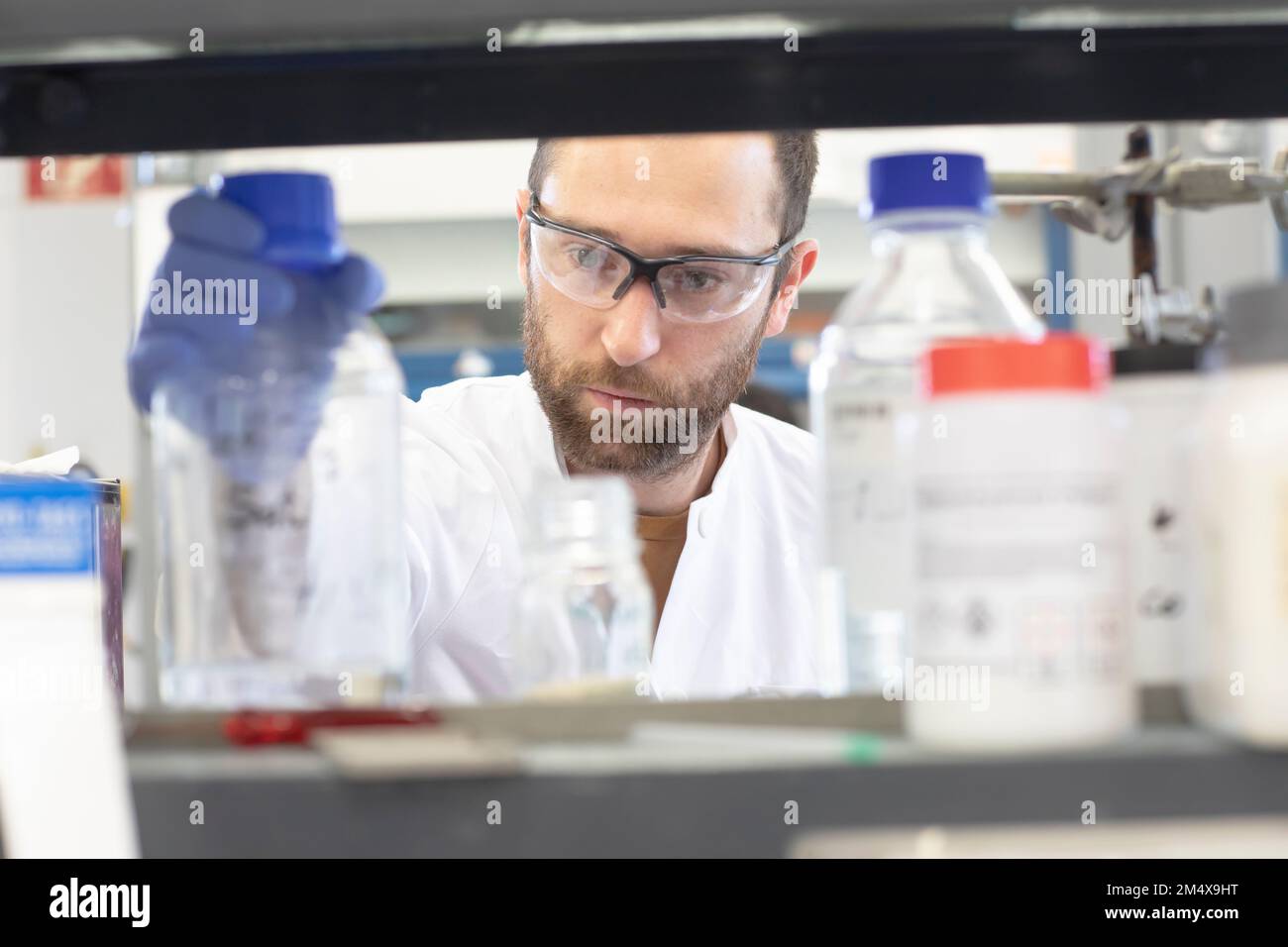 Scientist holding bottle seen through shelf in chemistry laboratory ...