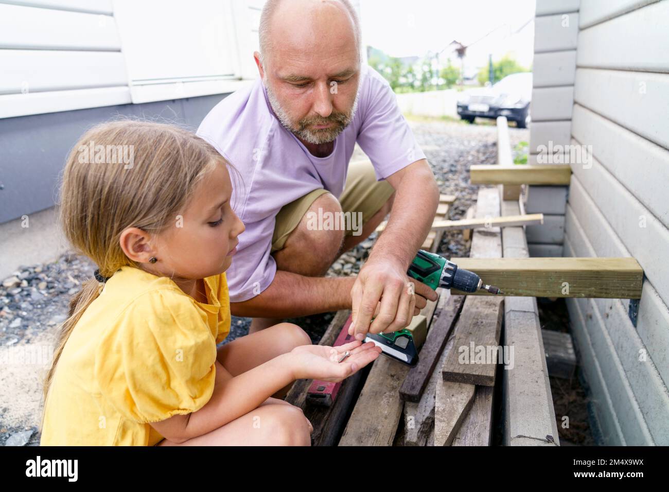 Father and daughter building wooden wall crouching outside house Stock ...