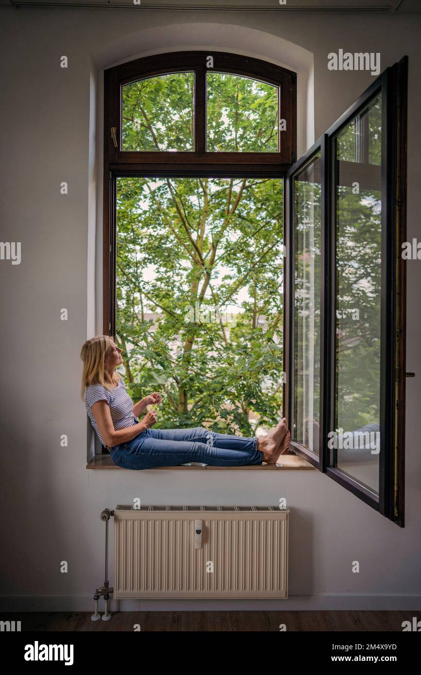 Contemplative mature woman sitting on window sill at home Stock Photo ...
