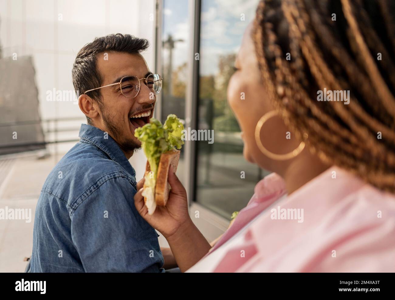 Happy young woman sharing sandwich with man at footpath Stock Photo - Alamy