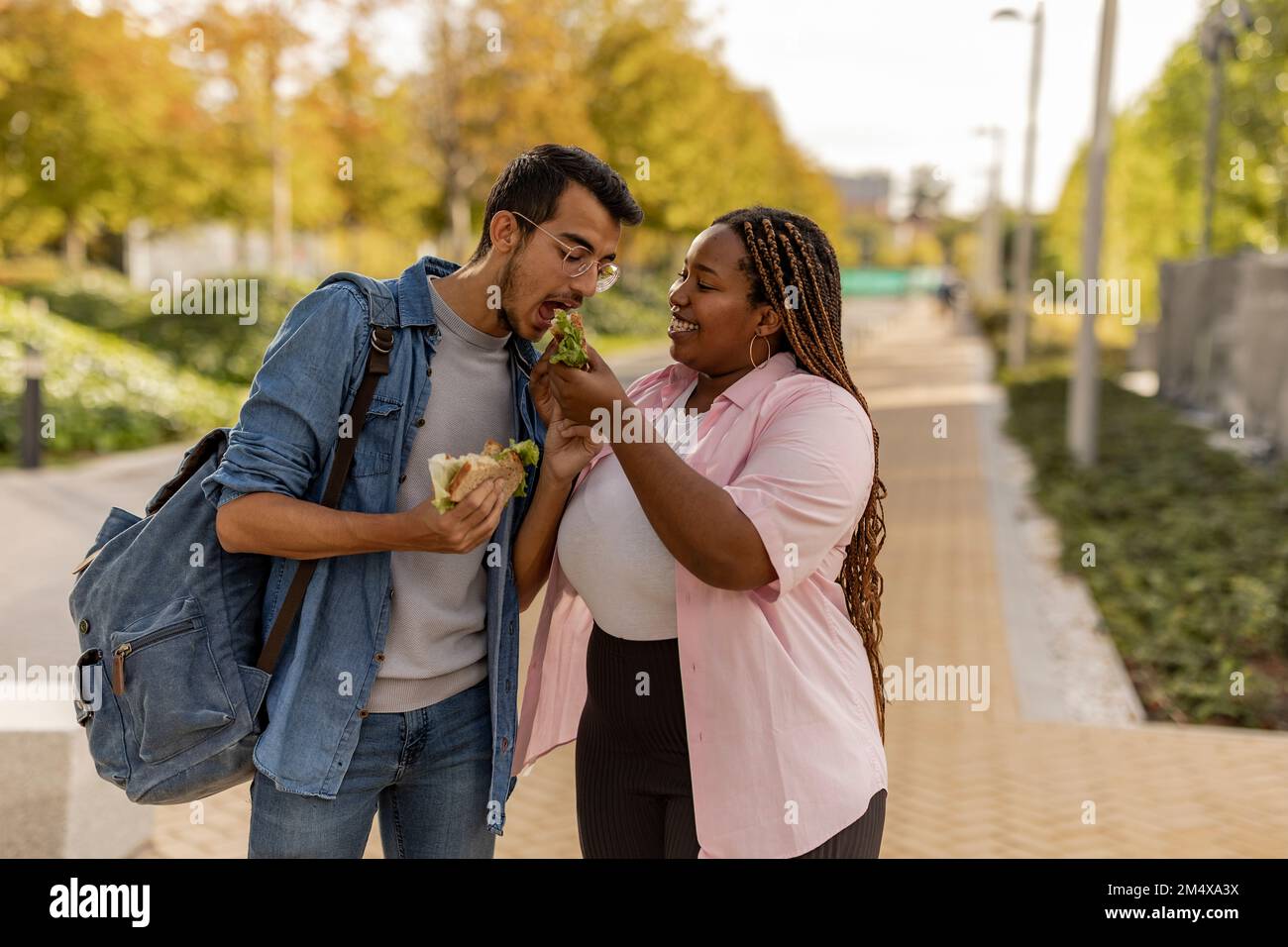 Young woman sharing sandwich with boyfriend at footpath Stock Photo - Alamy