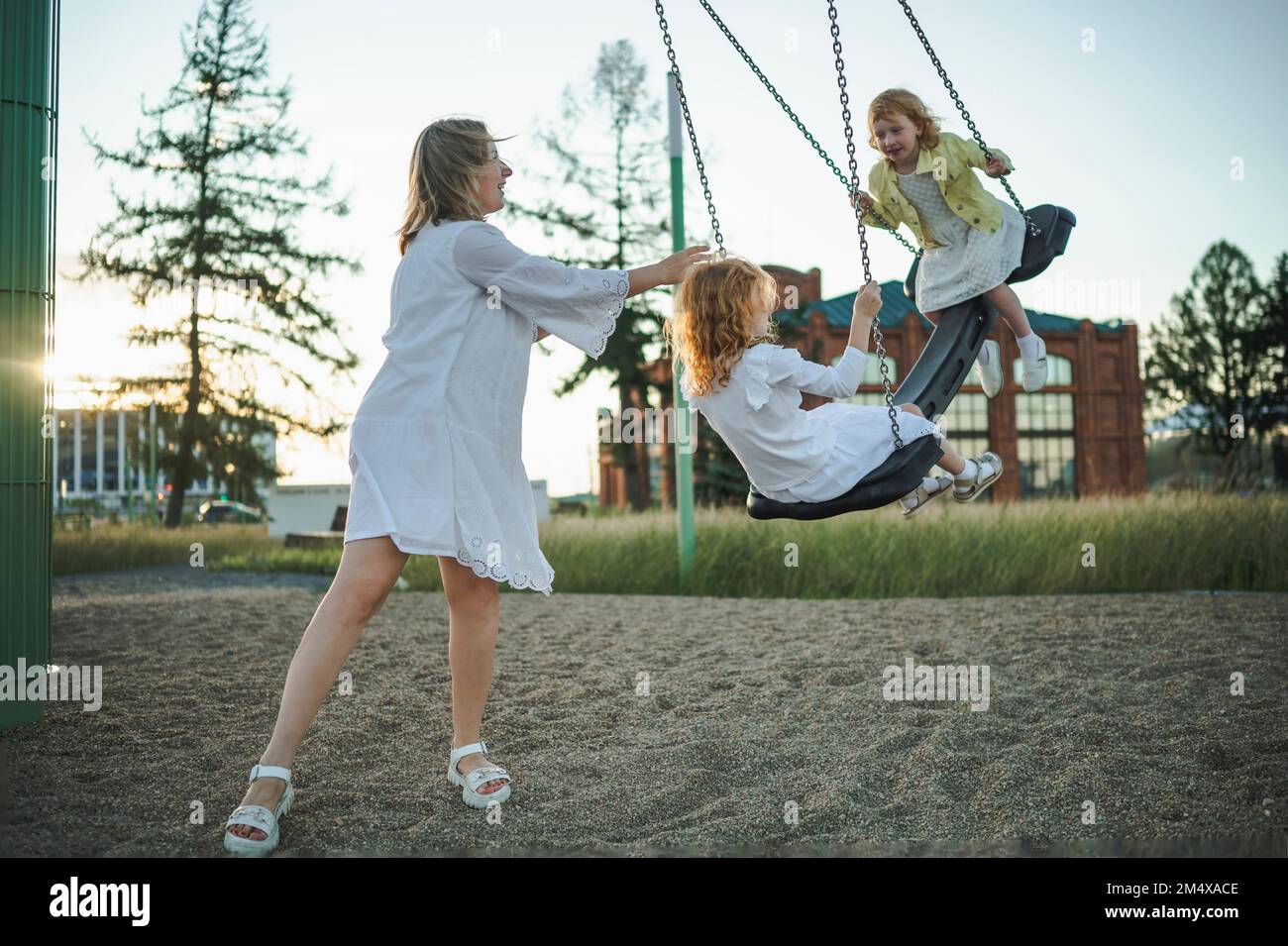 Happy mother enjoying with daughters swinging on swing at park Stock Photo - Alamy