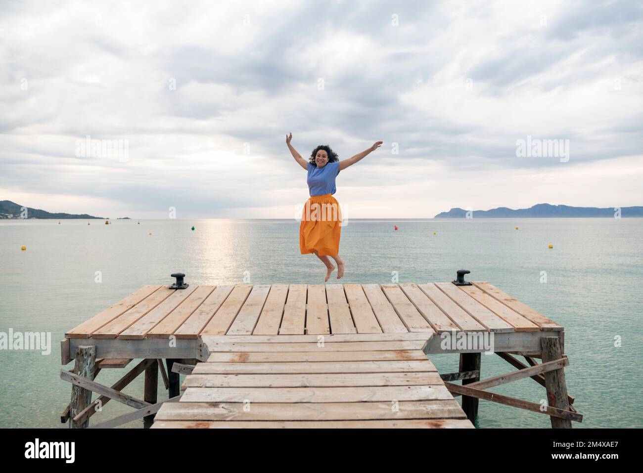 Happy woman jumping on jetty in front of sea Stock Photo - Alamy