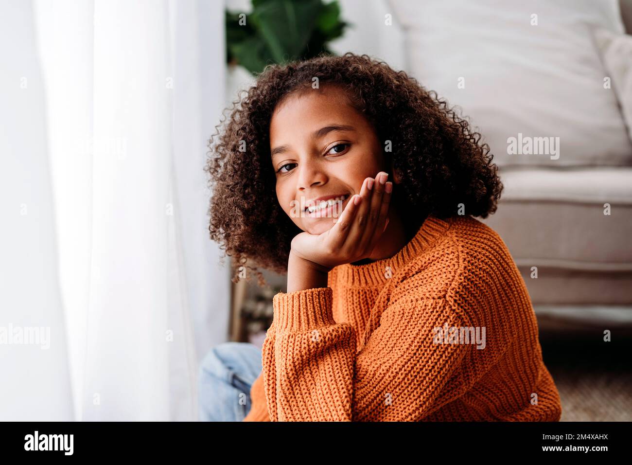 Happy cute girl sitting with hand on chin at home Stock Photo - Alamy