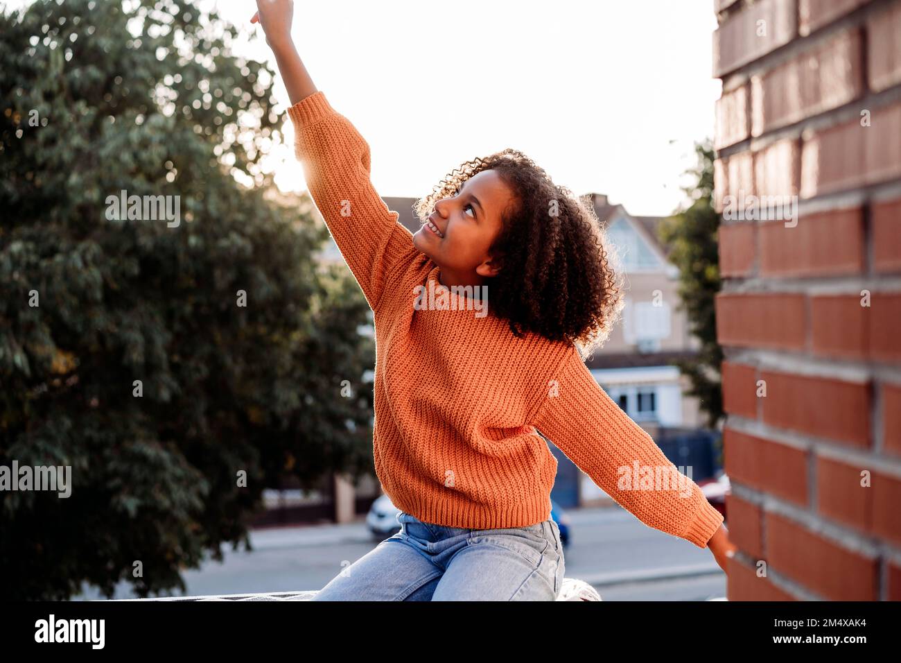Cute girl with arms raised sitting at terrace Stock Photo - Alamy
