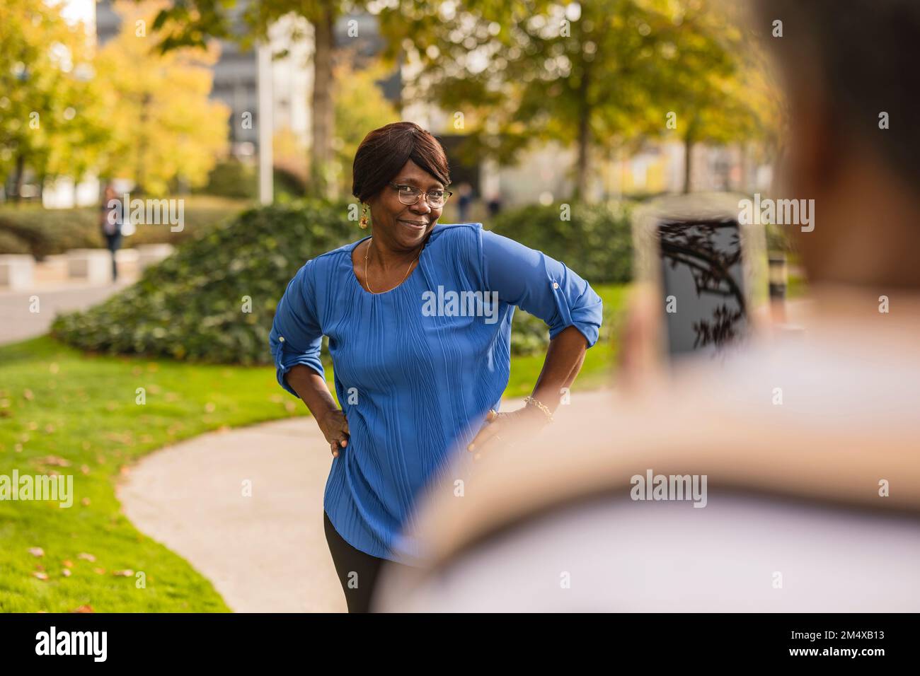 Man photographing woman standing with hands on hips at park Stock Photo ...