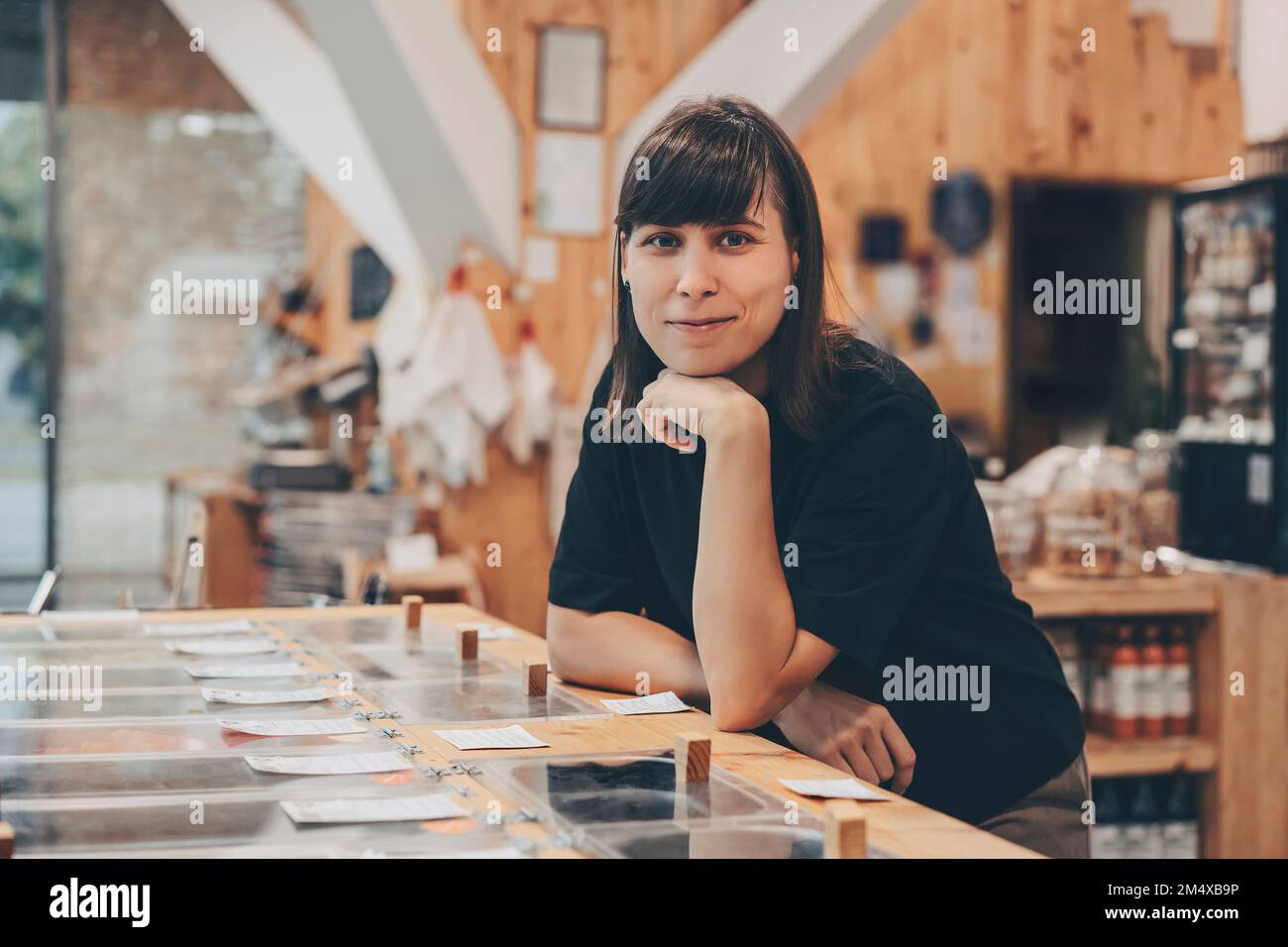 Smiling store owner leaning on counter in zero waste shop Stock Photo ...