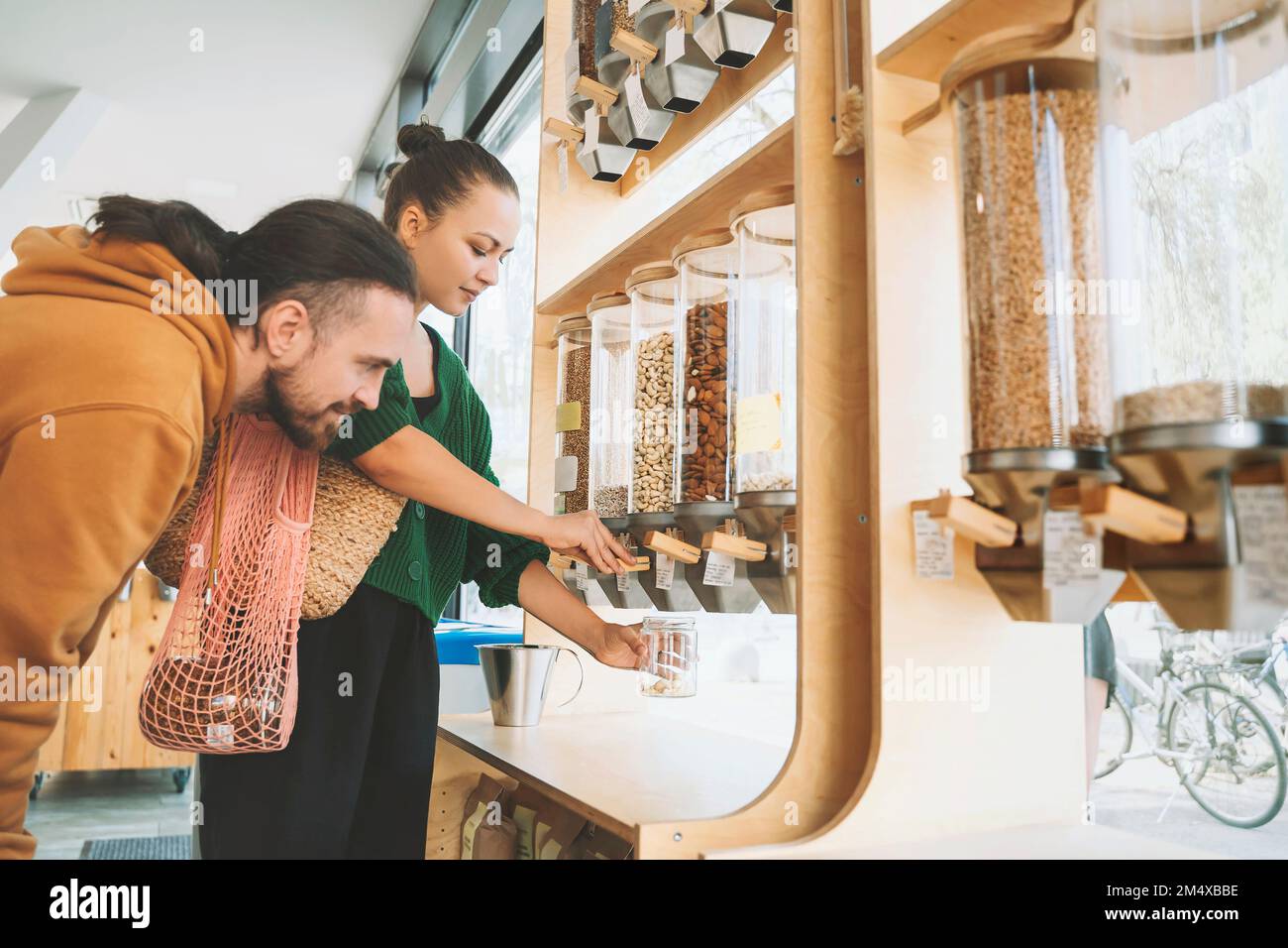 Man looking at woman filling mason jar under food dispenser at zero ...