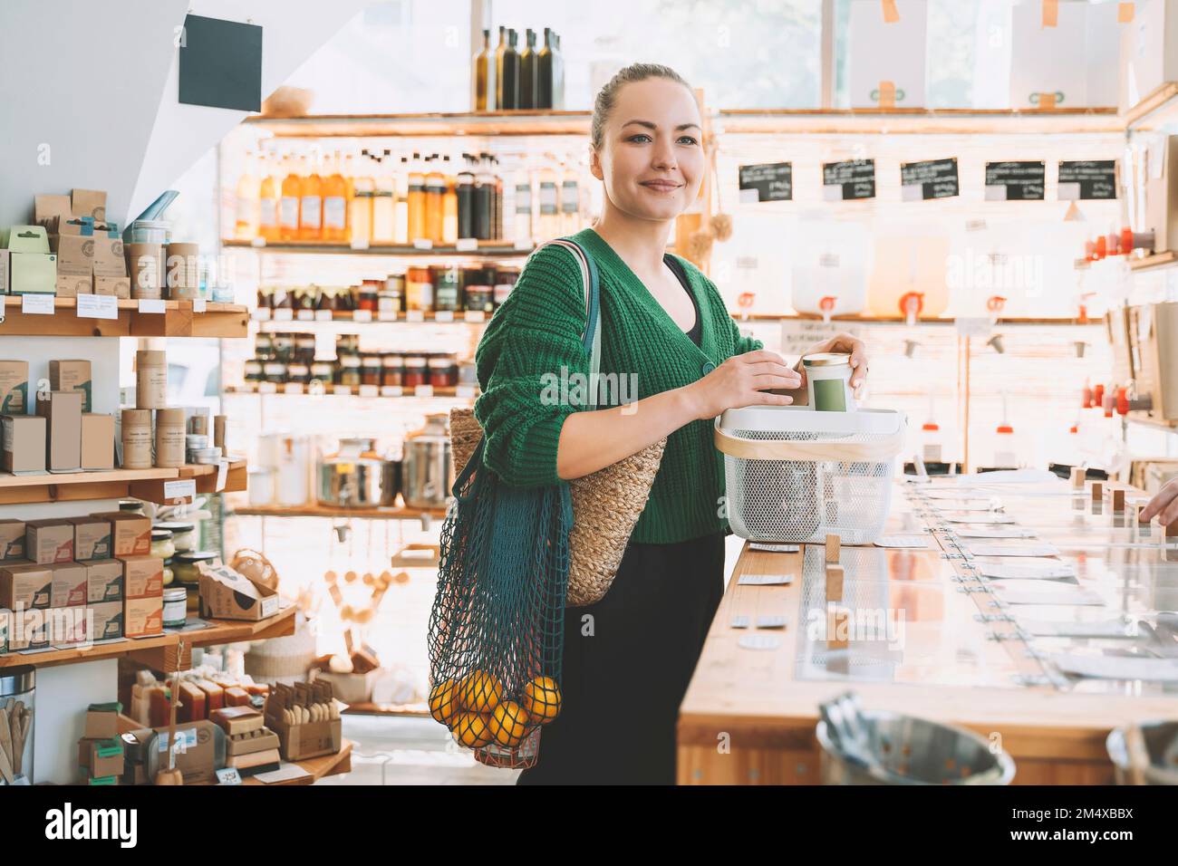 Smiling thoughtful customer with shopping basket on counter in ...