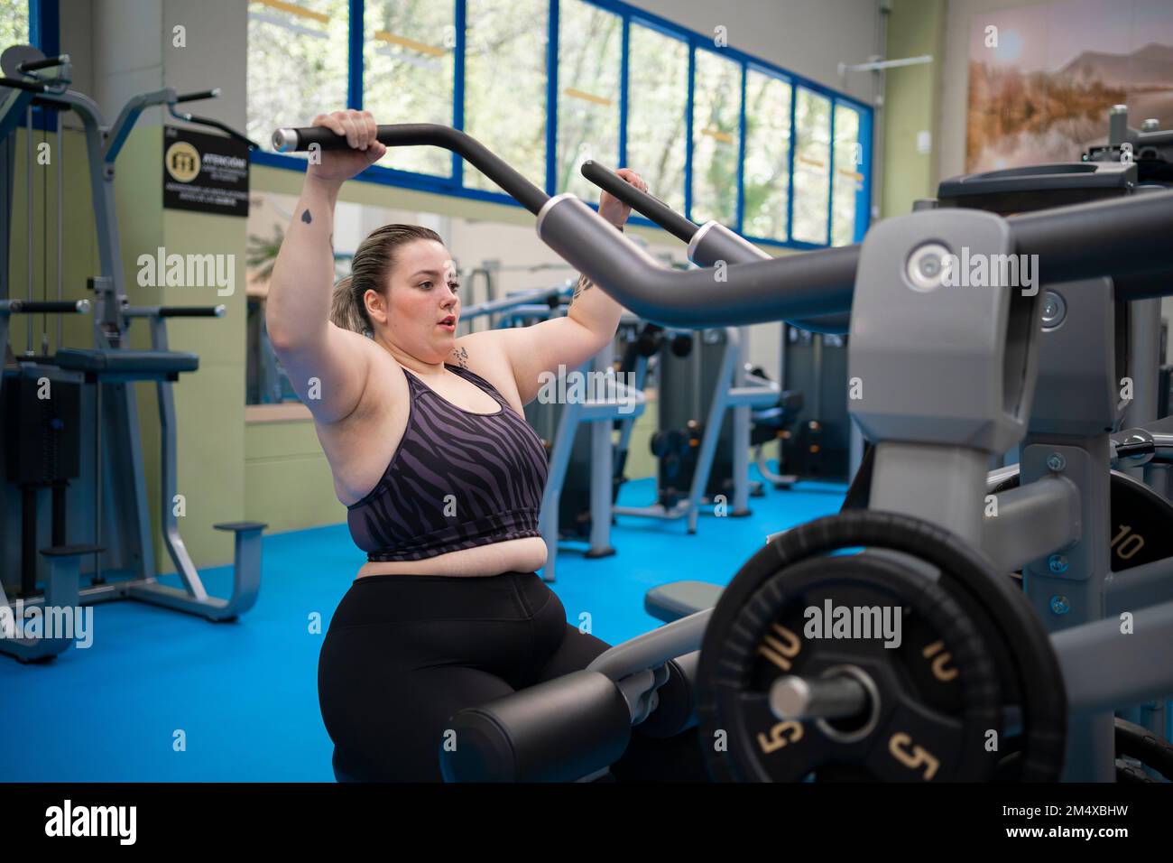 Overweight woman doing shoulder exercise in gym Stock Photo - Alamy