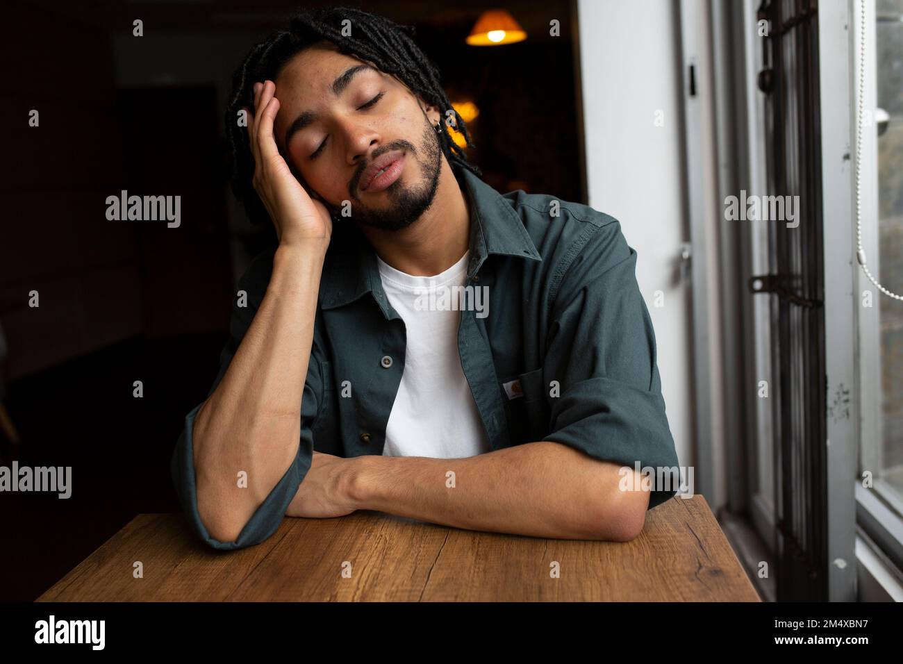 Tired man leaning on elbow at table near window in home Stock Photo - Alamy