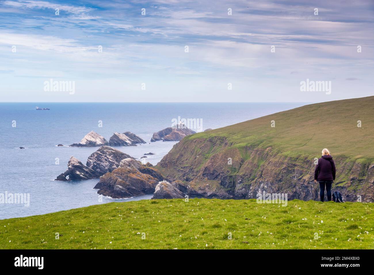 UK, Scotland, Unst, Female hiker standing on clifftop looking toward ...