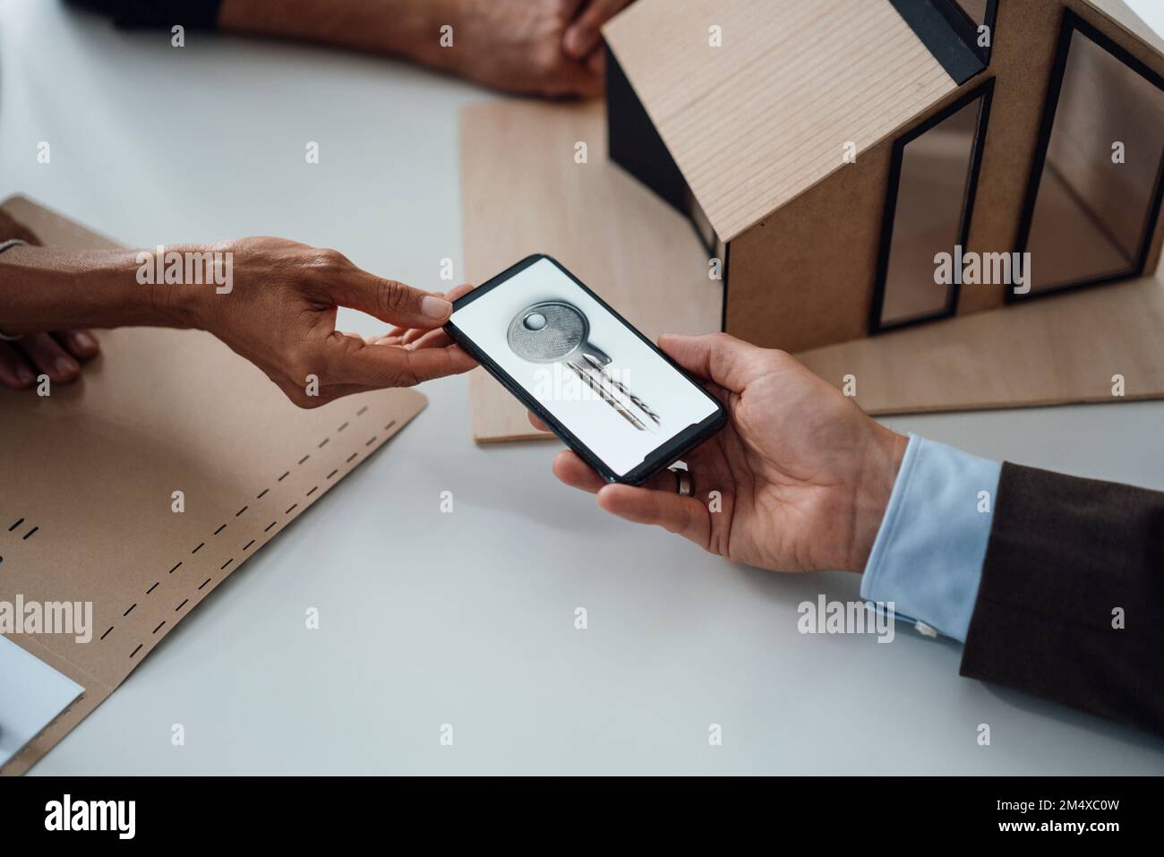 Cropped hands of real estate agent giving mobile phone with house key ...