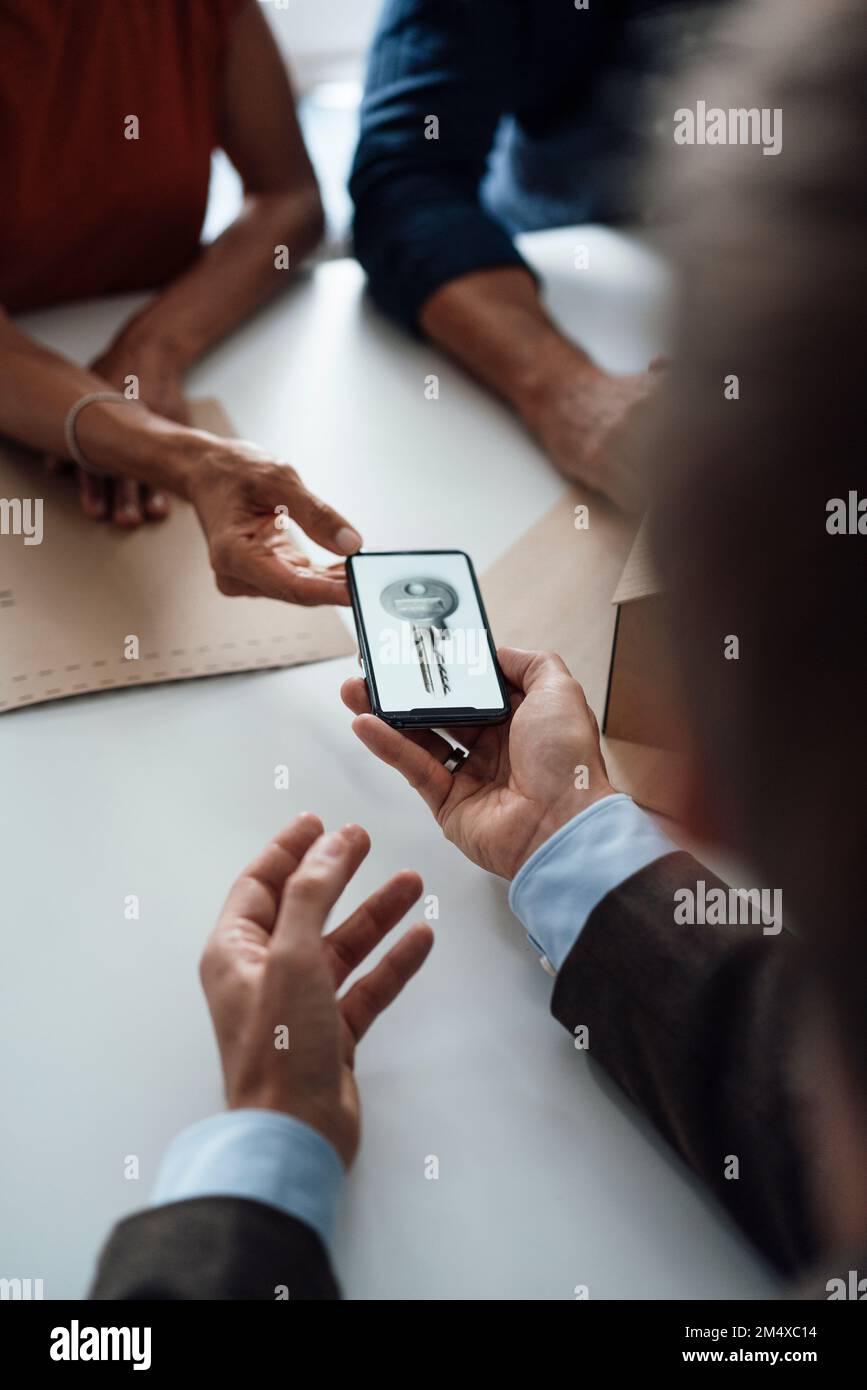 Hands of real estate agent giving mobile phone with house key on screen ...