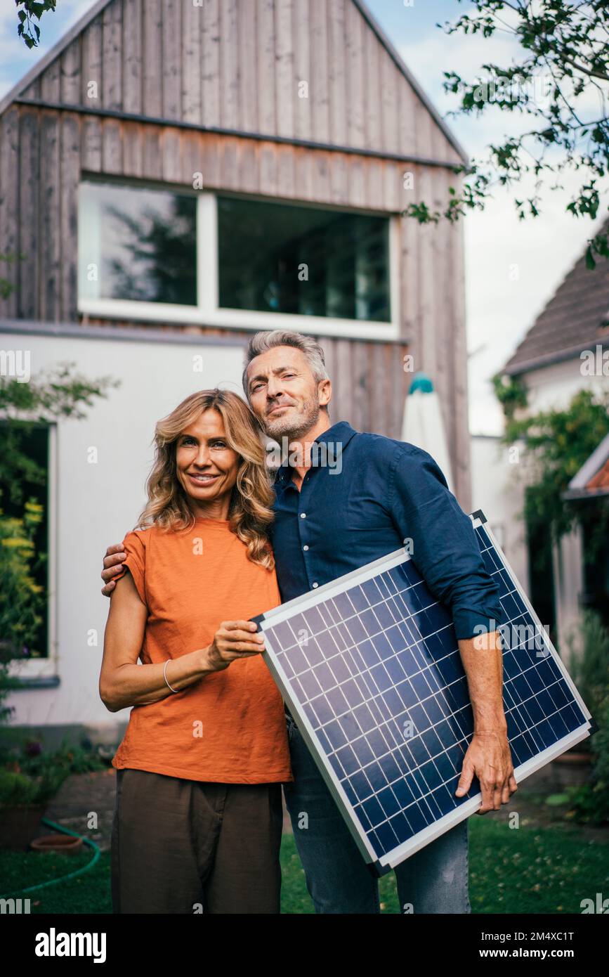 Smiling mature woman with man holding solar panel standing in front of ...