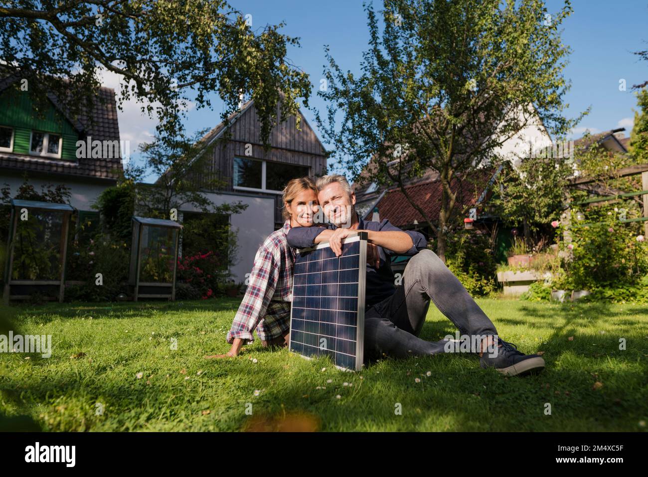 Smiling couple sitting with solar panel on grass in back yard Stock ...