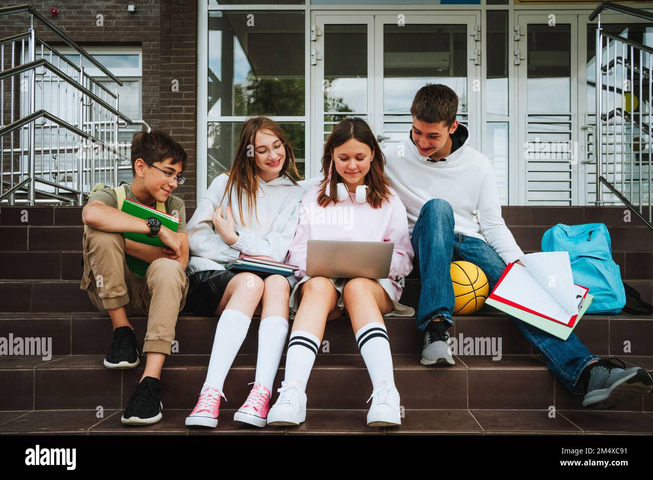 Girl doing homework over laptop by friends sitting on steps at school ...