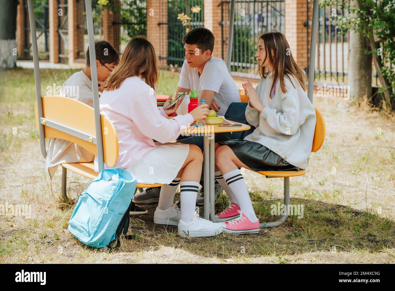 Teenage friends sitting in schoolyard at table having lunch Stock Photo ...