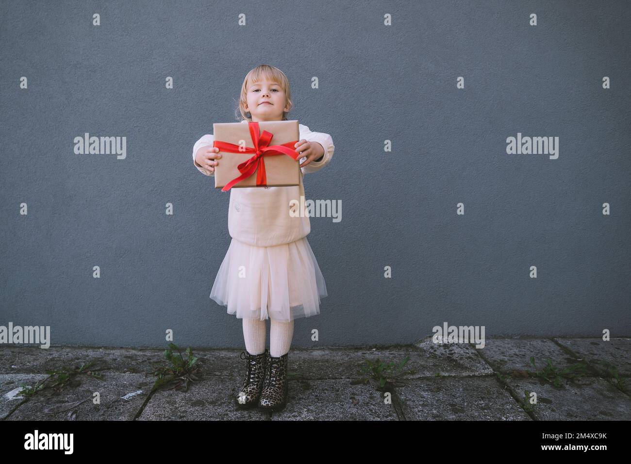 Girl holding gift box standing in front of concrete wall Stock Photo ...