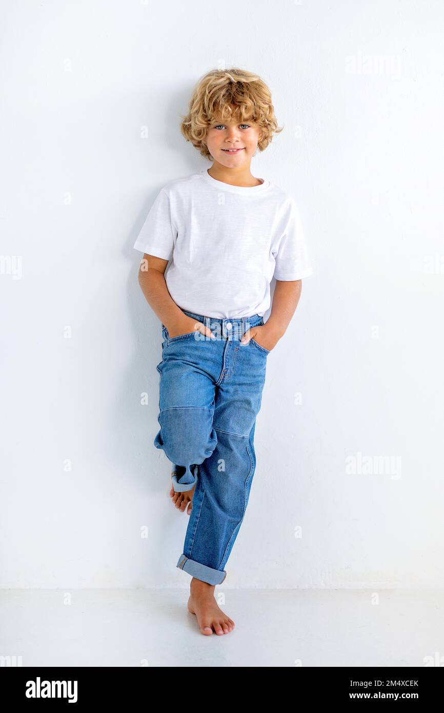 Cute boy with hands in pockets leaning on white background Stock Photo ...