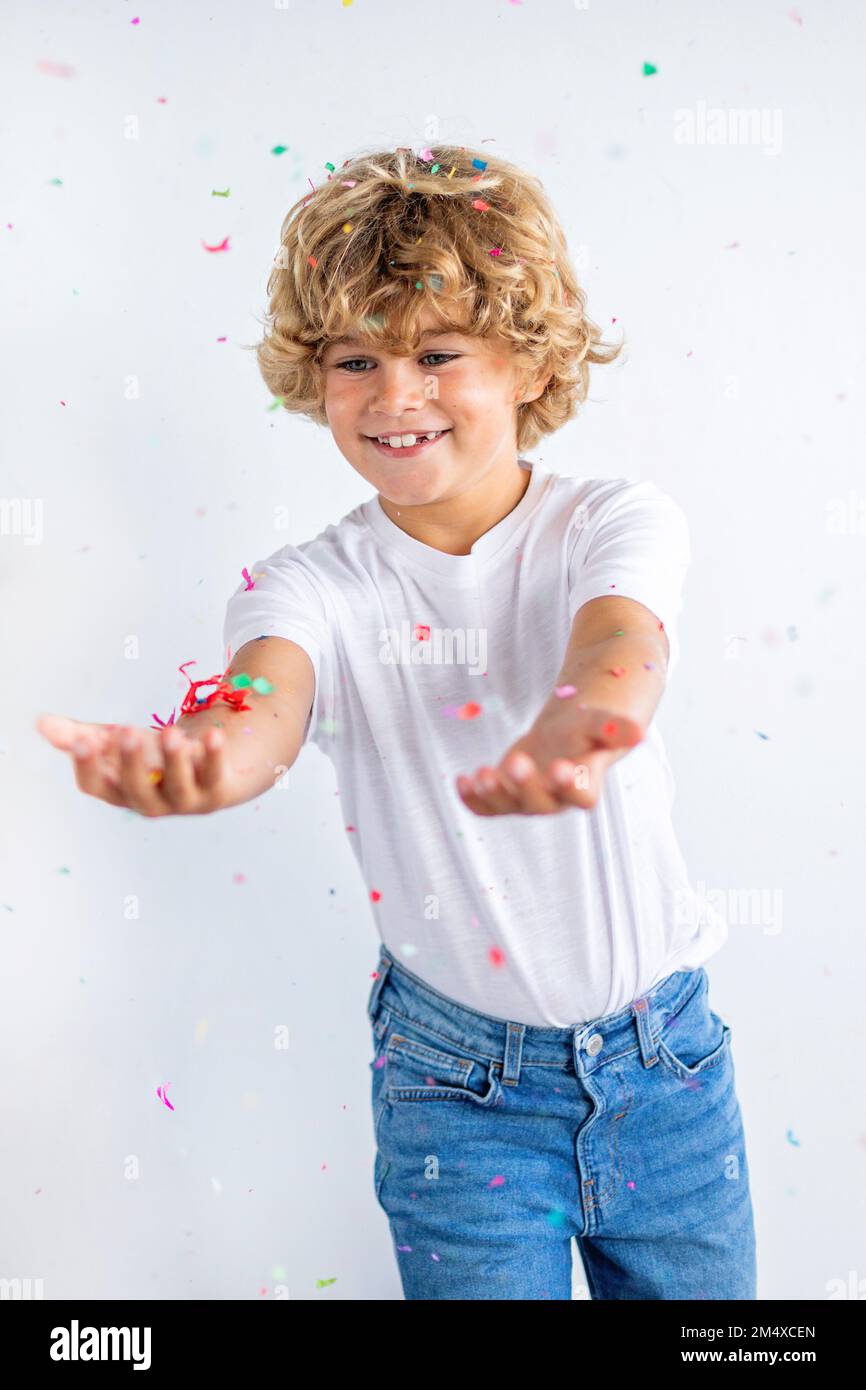 Smiling boy playing with confetti against white background Stock Photo ...