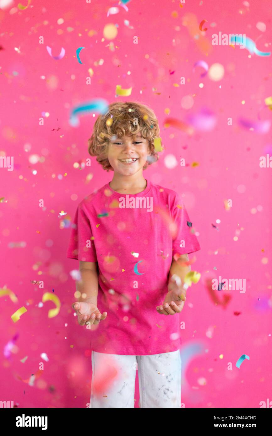 Cheerful boy playing with confetti against pink background Stock Photo ...