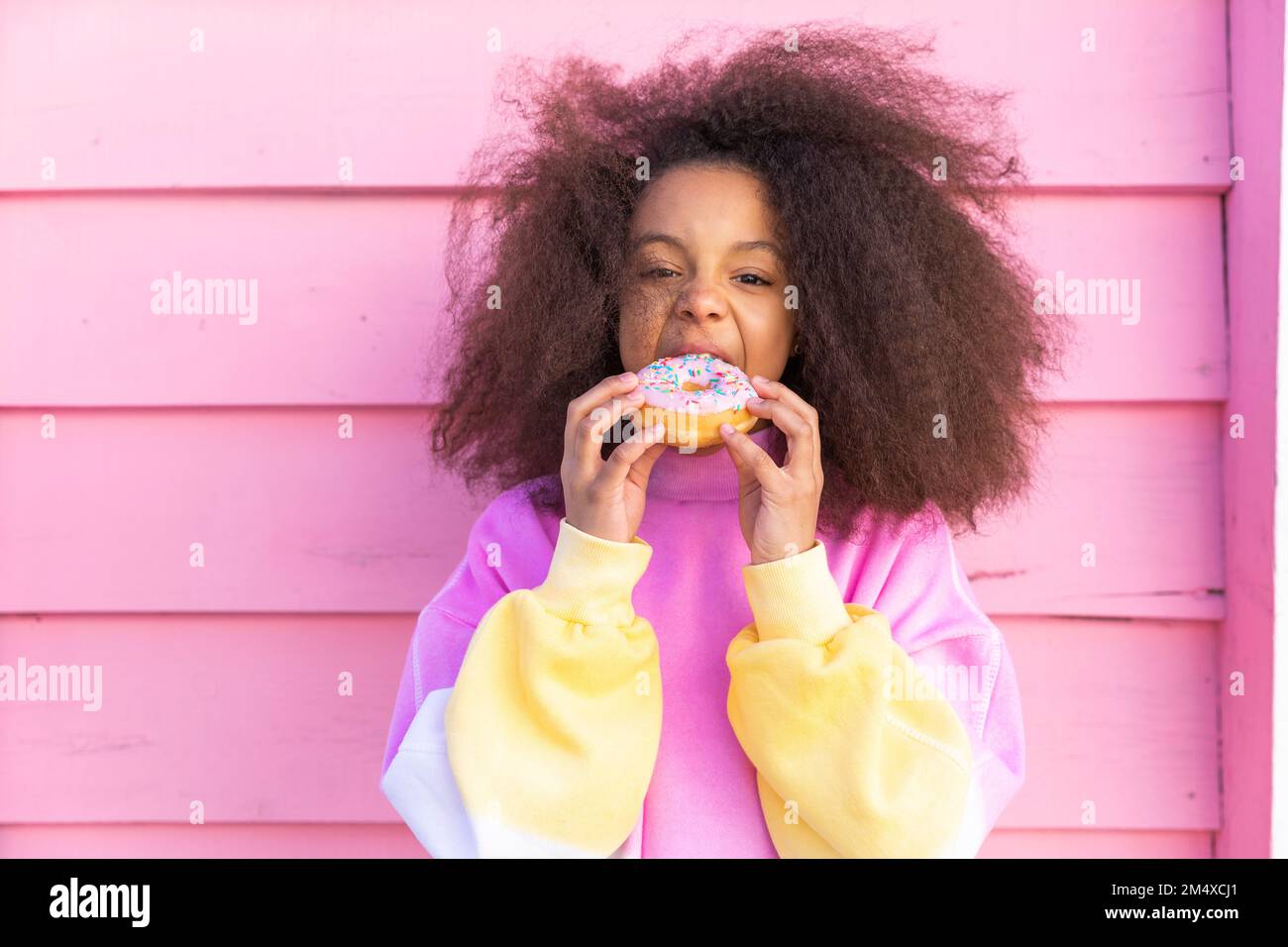 Hungry girl eating doughnut in front of pink wall Stock Photo - Alamy