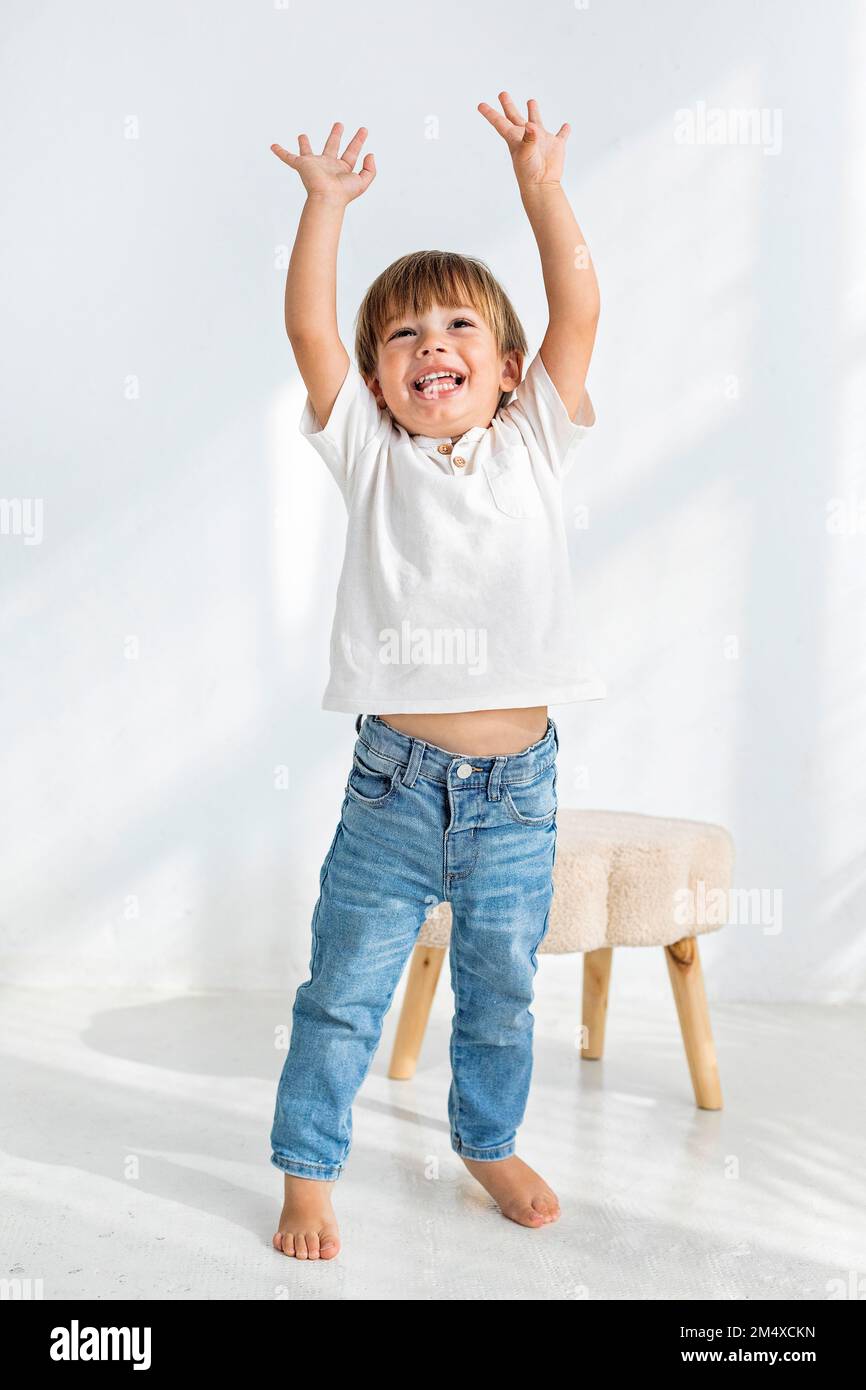 Boy with arms raised standing in front of wall at home Stock Photo - Alamy