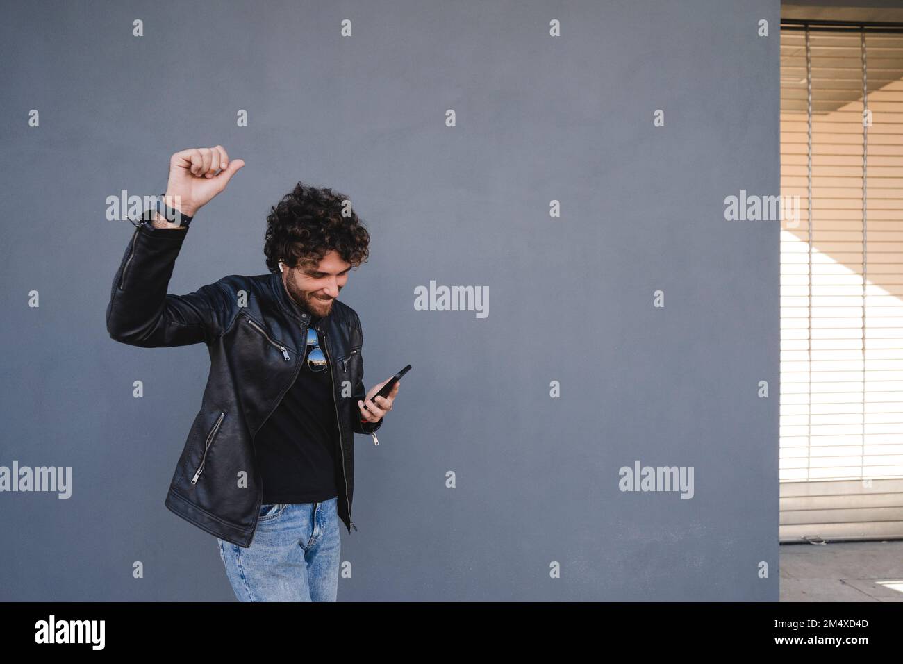 Happy man with hand raised holding mobile phone enjoying in front of ...