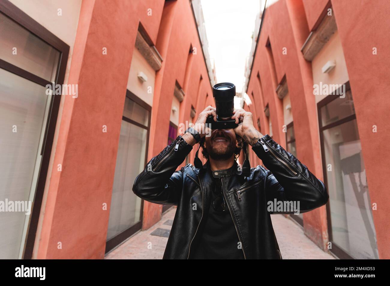 Happy man photographing through camera amidst buildings Stock Photo - Alamy