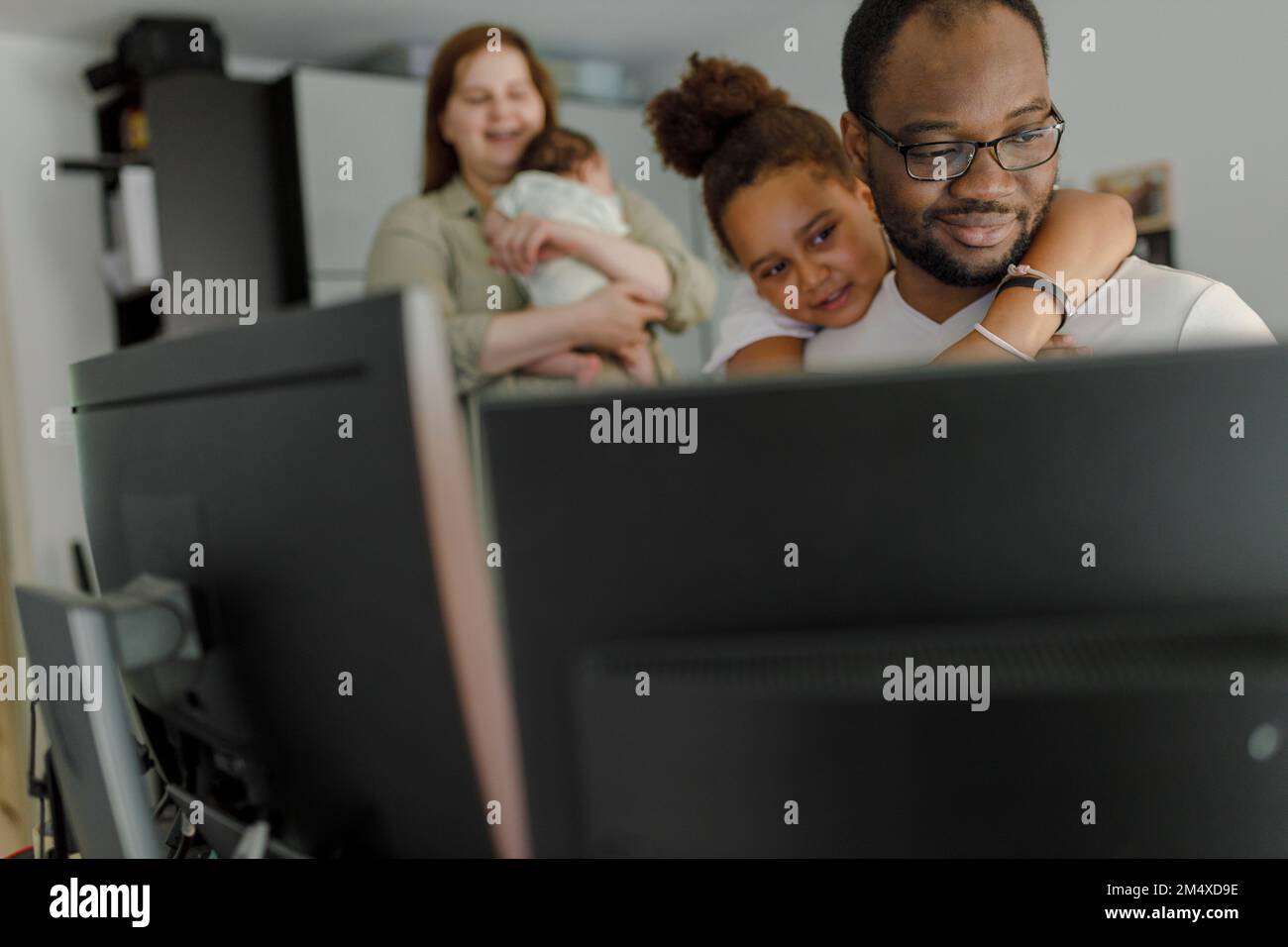 Smiling man working through computer with daughter embracing from ...