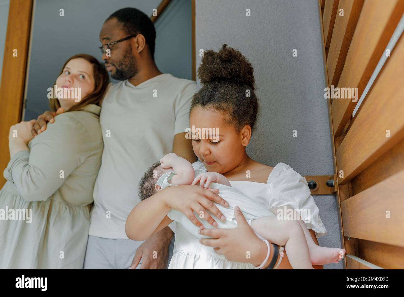 Girl carrying baby girl with parents standing at doorway Stock Photo ...